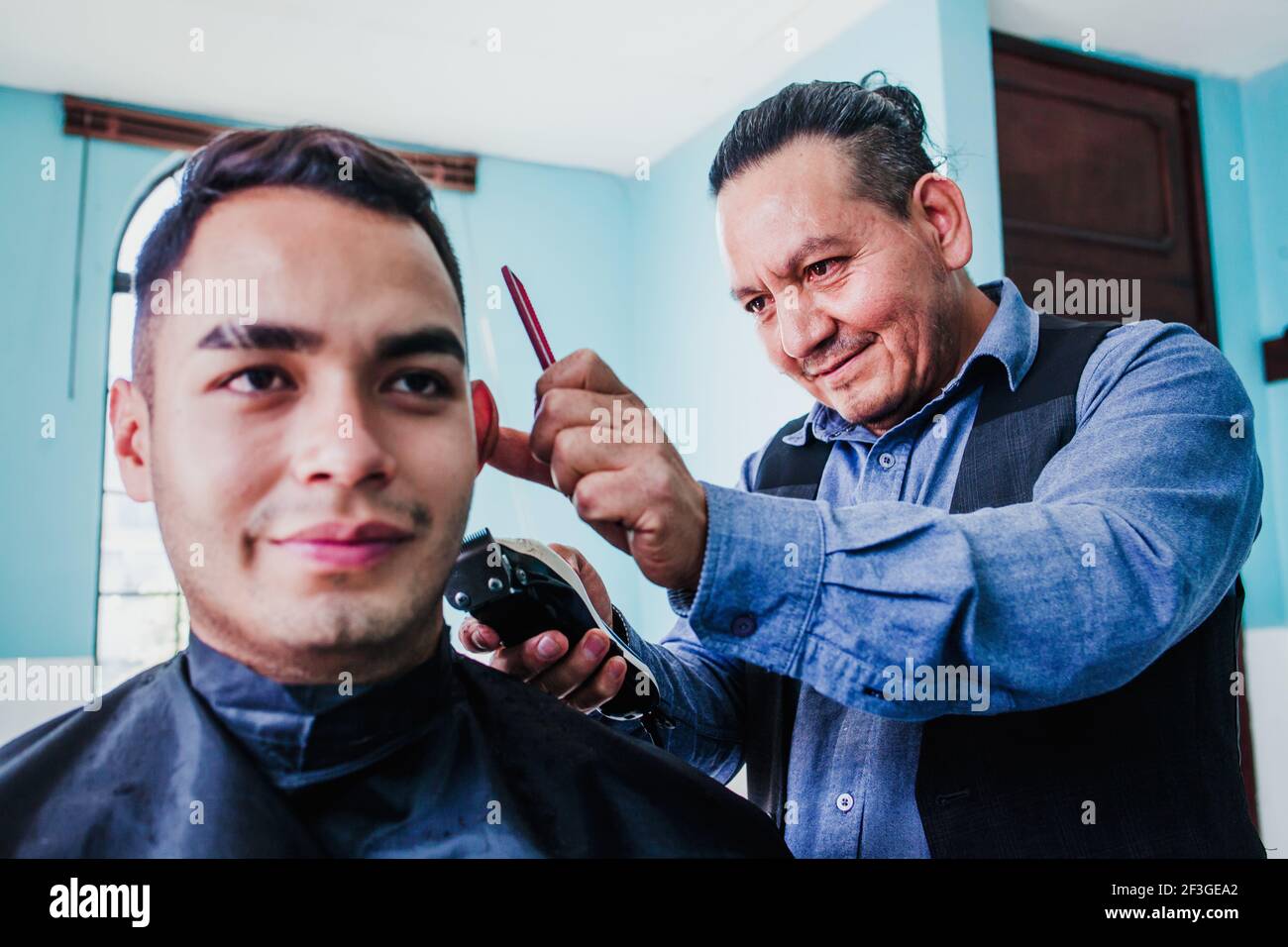 latin man stylist cutting hair to a client in a barber shop in Mexico ...