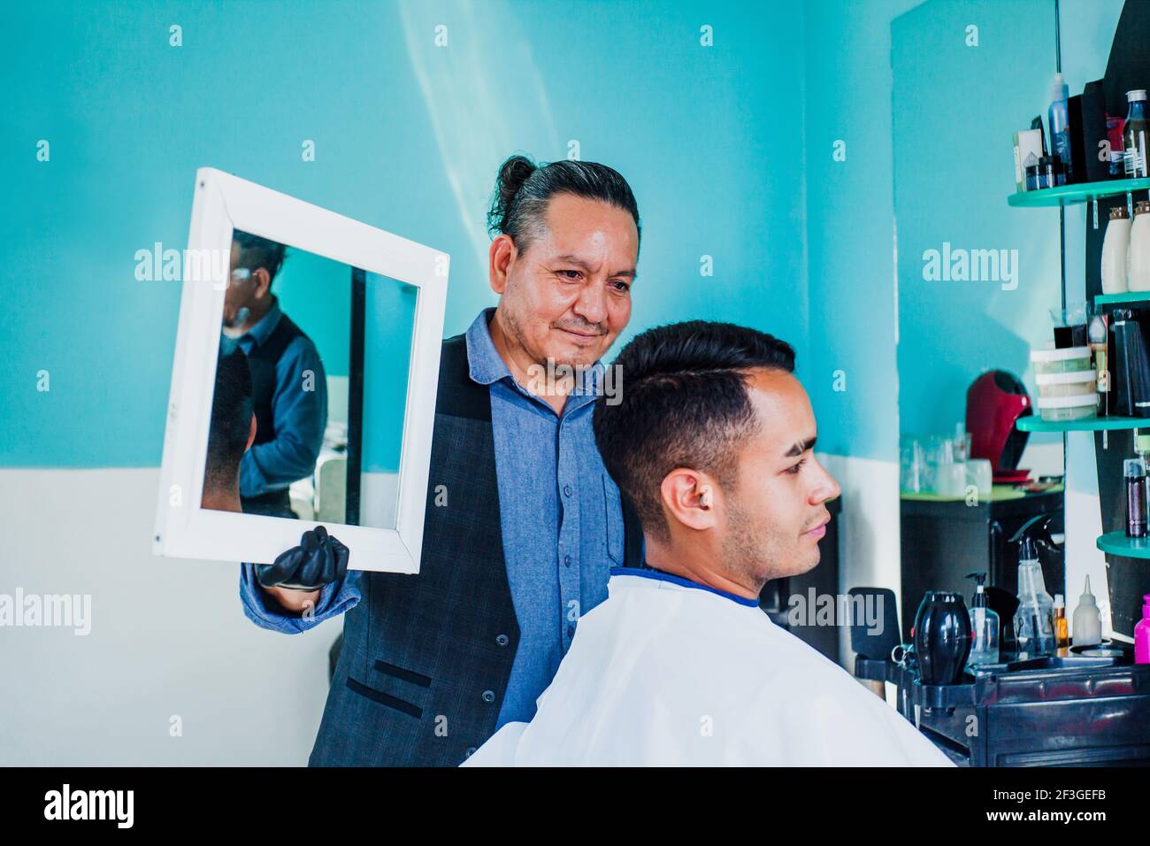 latin man stylist cutting hair to a client and holding a mirror in a ...