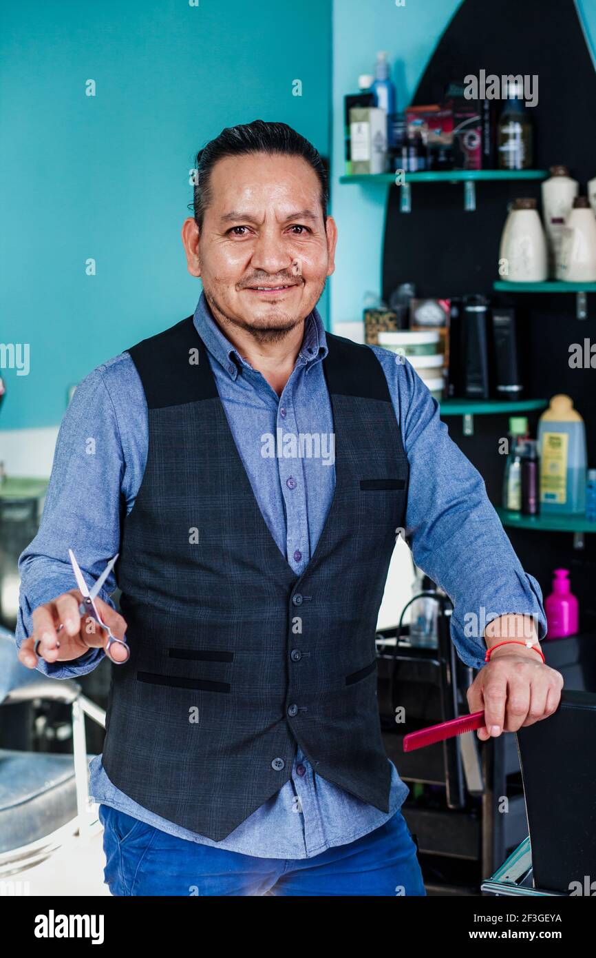 Portrait of latin man barber holding equipments in hand, looking at ...