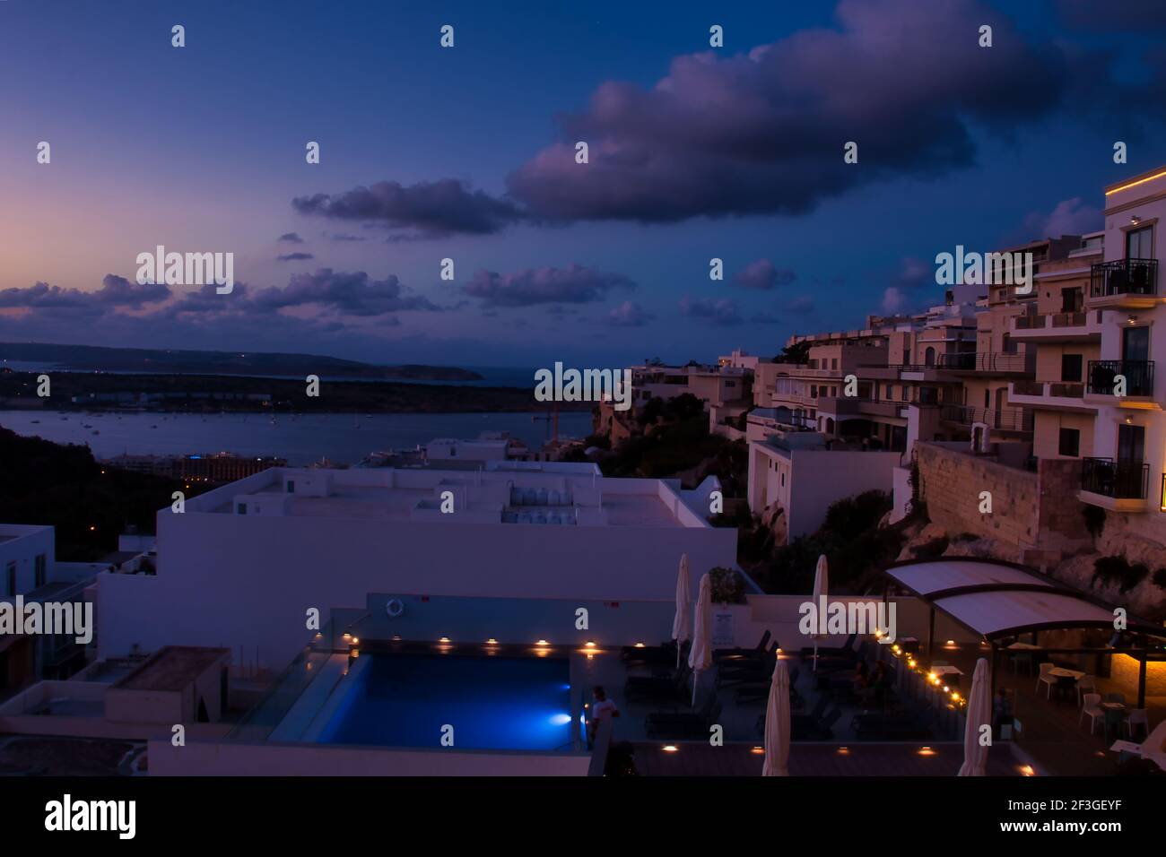 Pool and buildings lit up during blue hour at a resort near the ocean ...