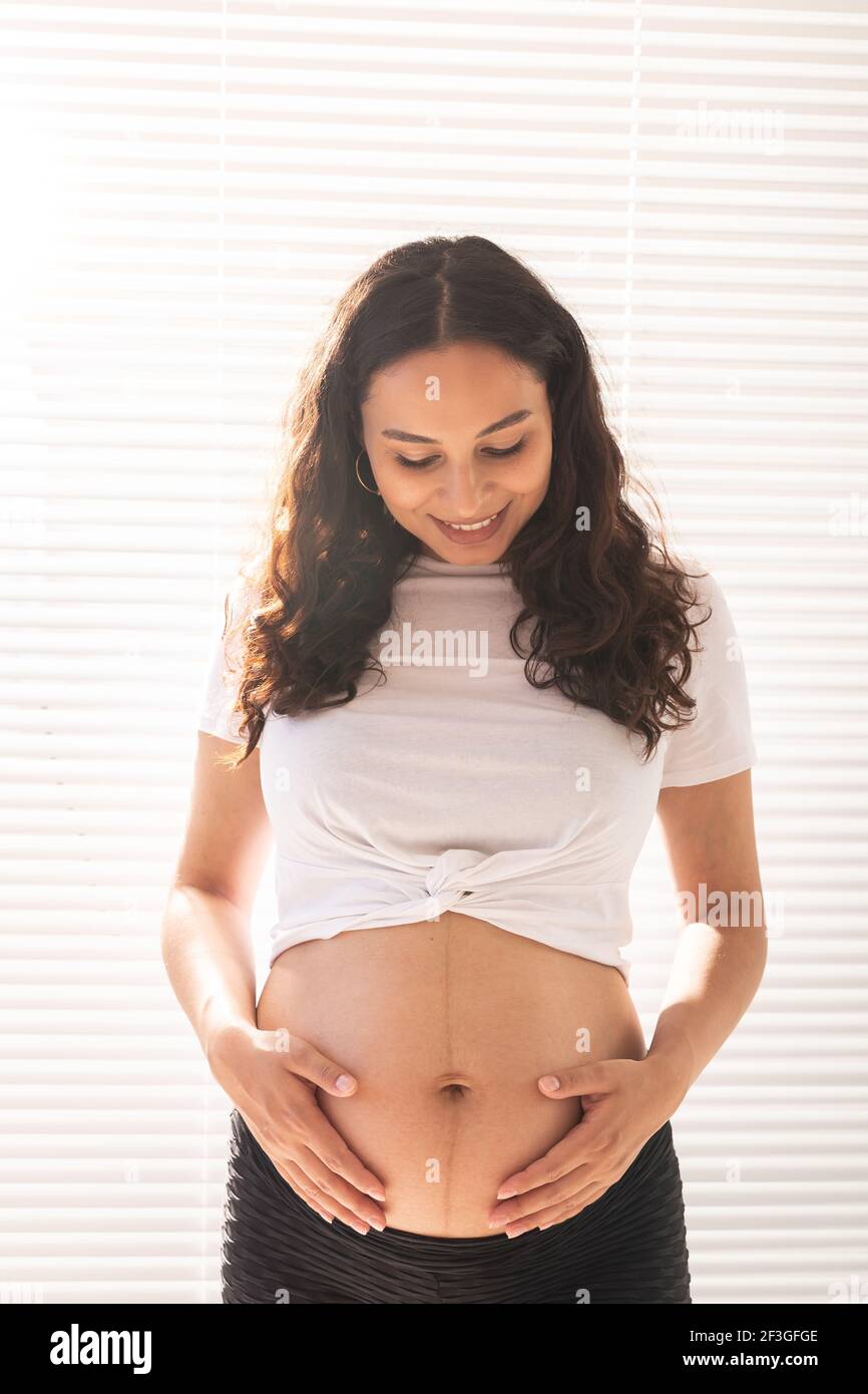 Smiling young beautiful pregnant woman touching her belly and rejoicing ...