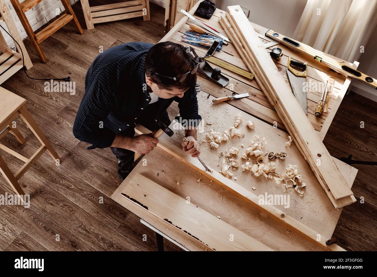 Middle-aged man carpenter working in a workshop with chisel and hammer ...