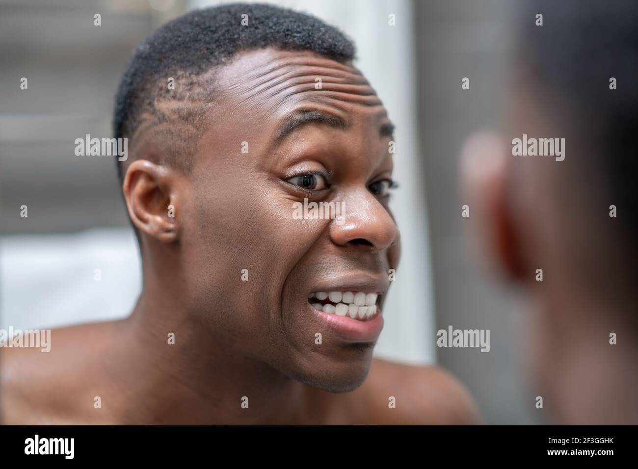 African american short-haired guy looking at himself in the mirror ...