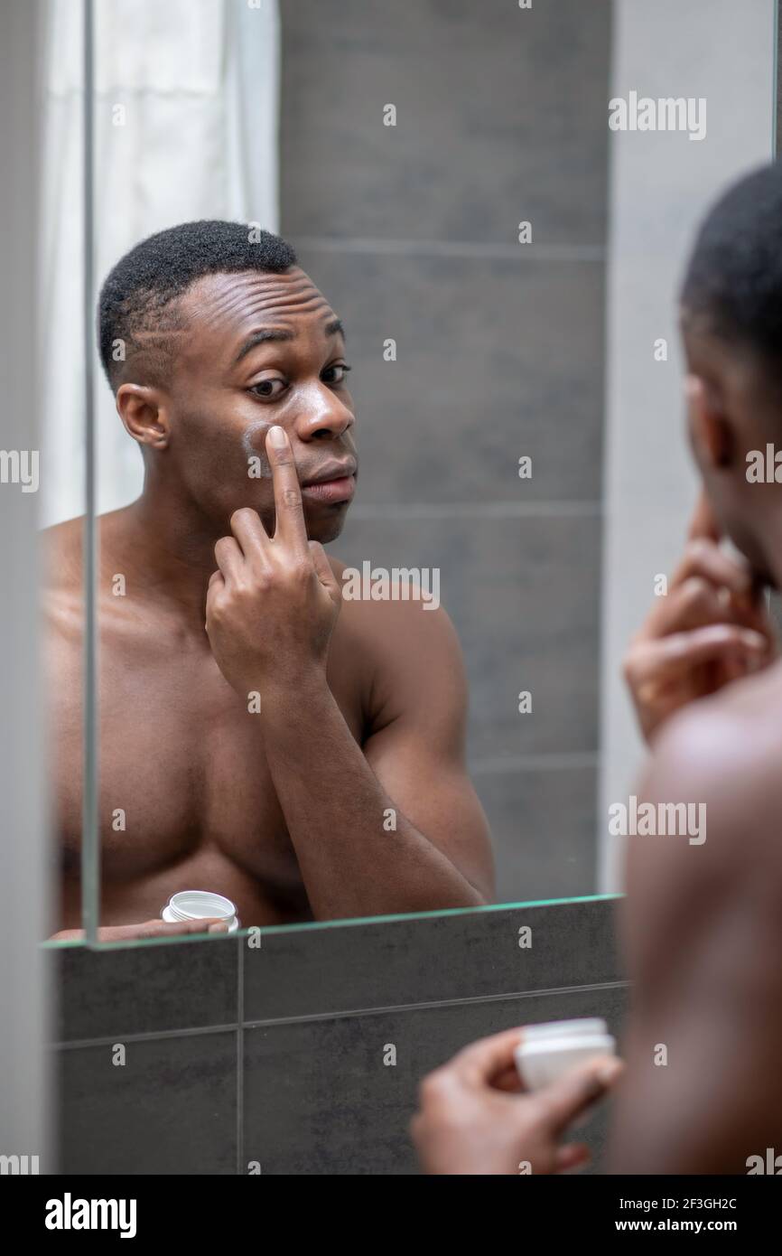 African American Short Haired Guy Applying Some Cream On His Face Stock