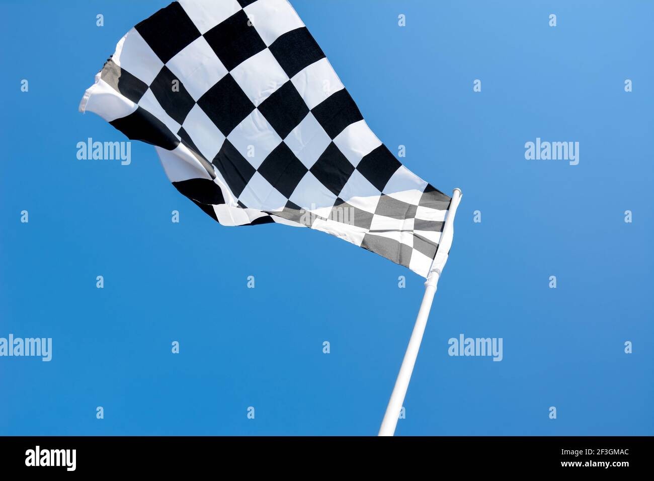 Checkered flag flying on blue sky background Stock Photo - Alamy