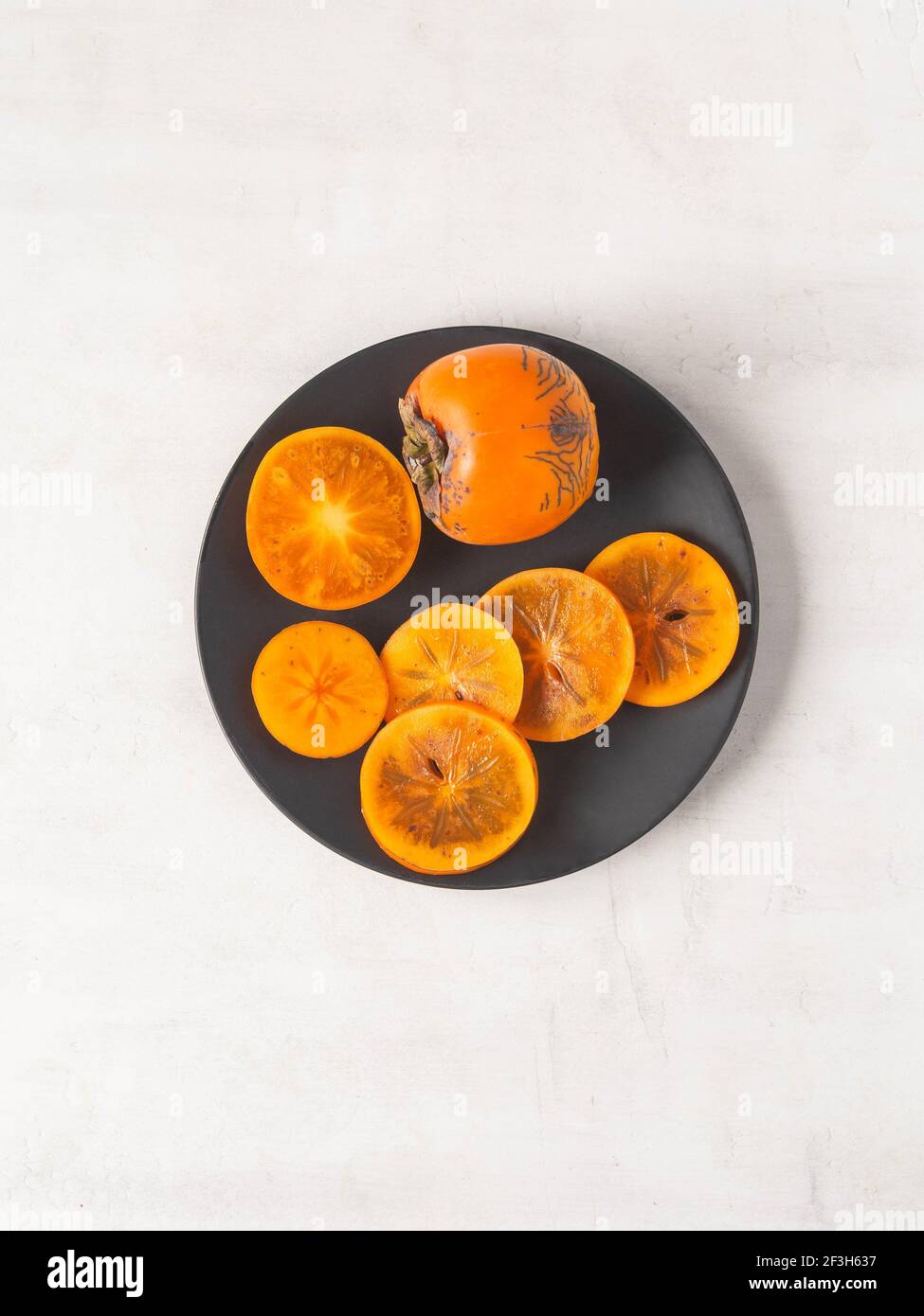 Ripe orange juicy persimmon slices and whole fruit on black plate on ...