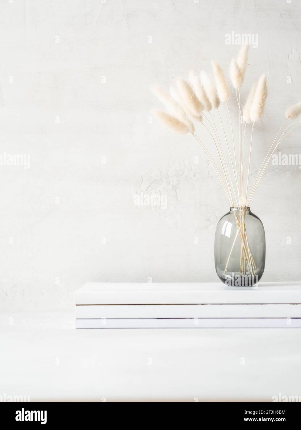 Still life of white dry lagurus flower in gray glass vase on stack of ...