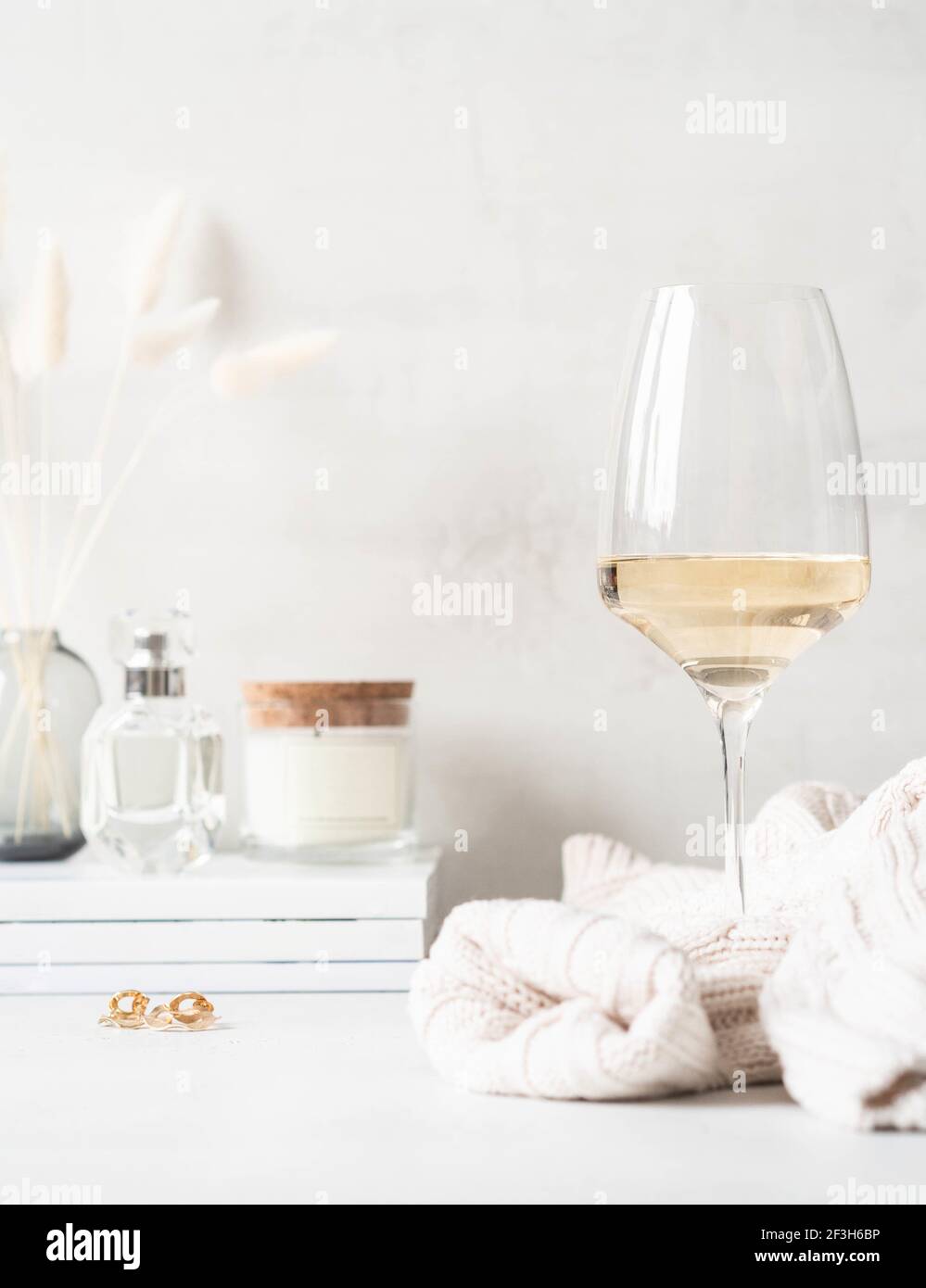 Modern feminine still life of glass of white wine, sweater and various ...