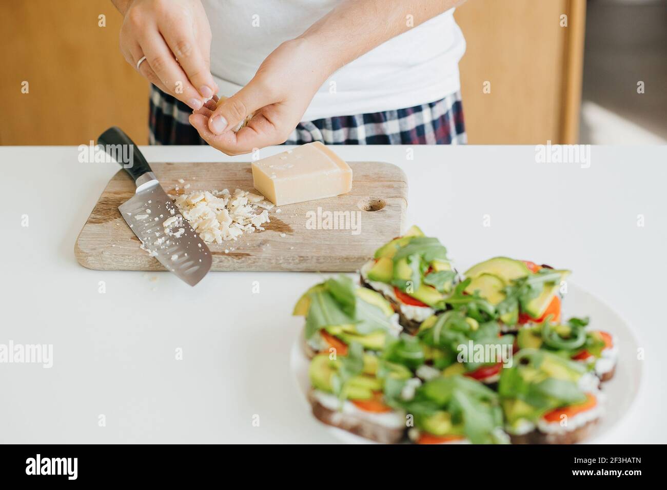 Young man making toasts with avocado, tomato, arugula, cheese in modern ...
