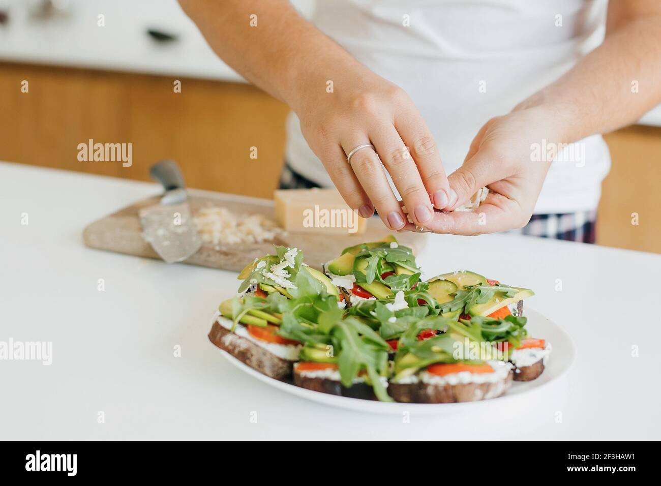 Young man making toasts with avocado, tomato, arugula, cheese in modern ...
