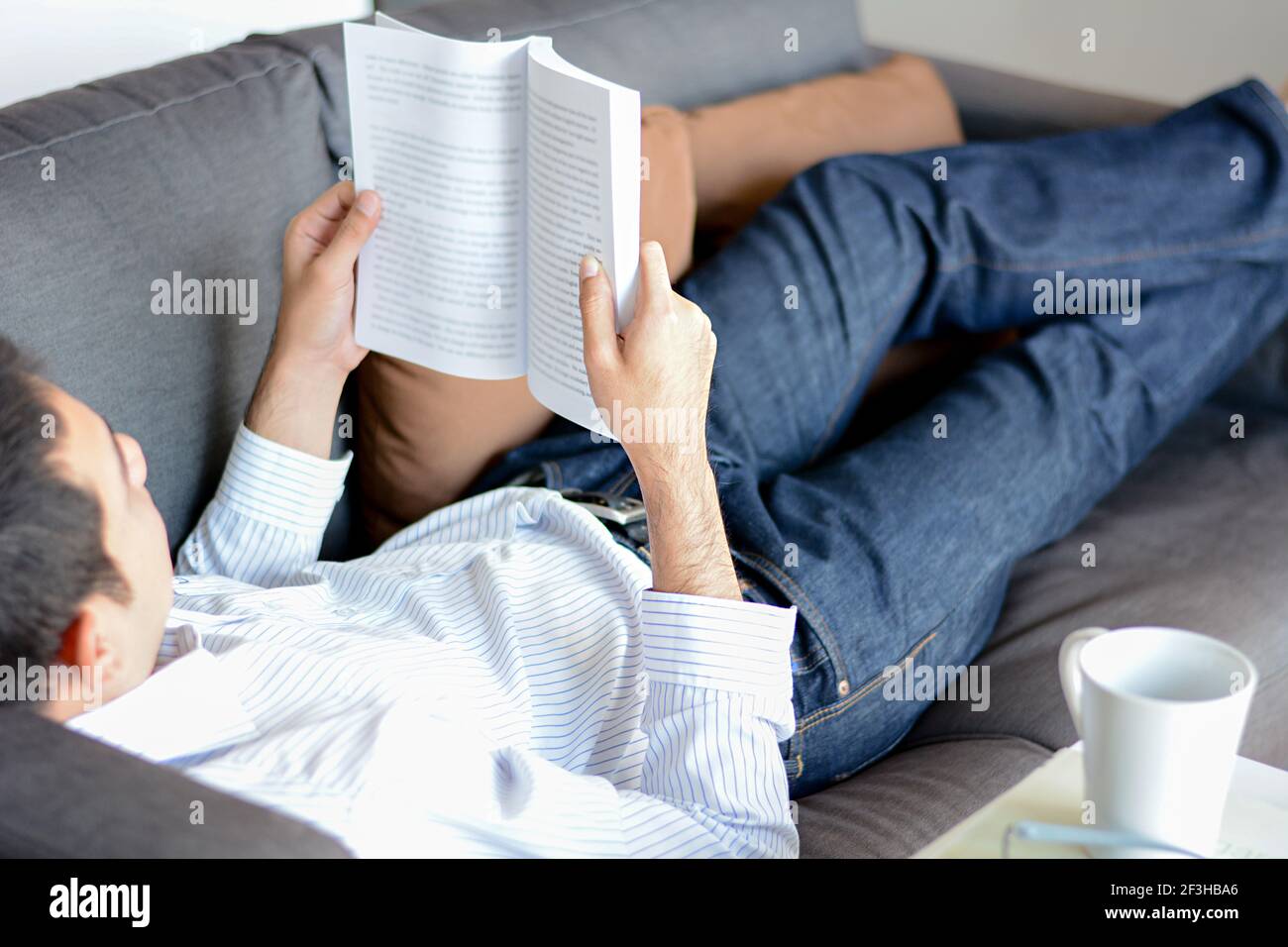 A man reading book while lying on the couch Stock Photo - Alamy