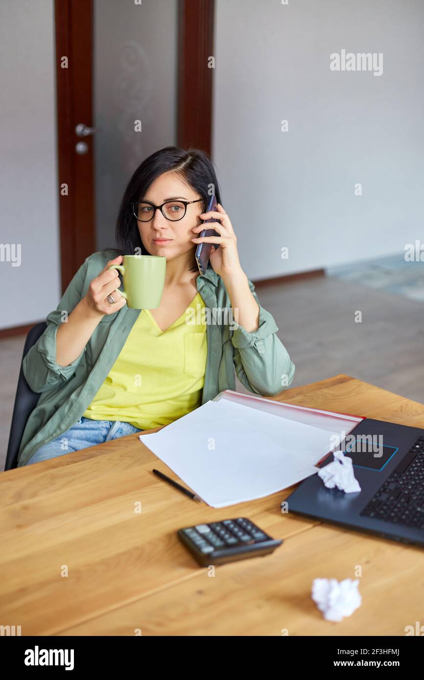 Stylish brunette woman in glasses sitting at wooden table with notepad ...