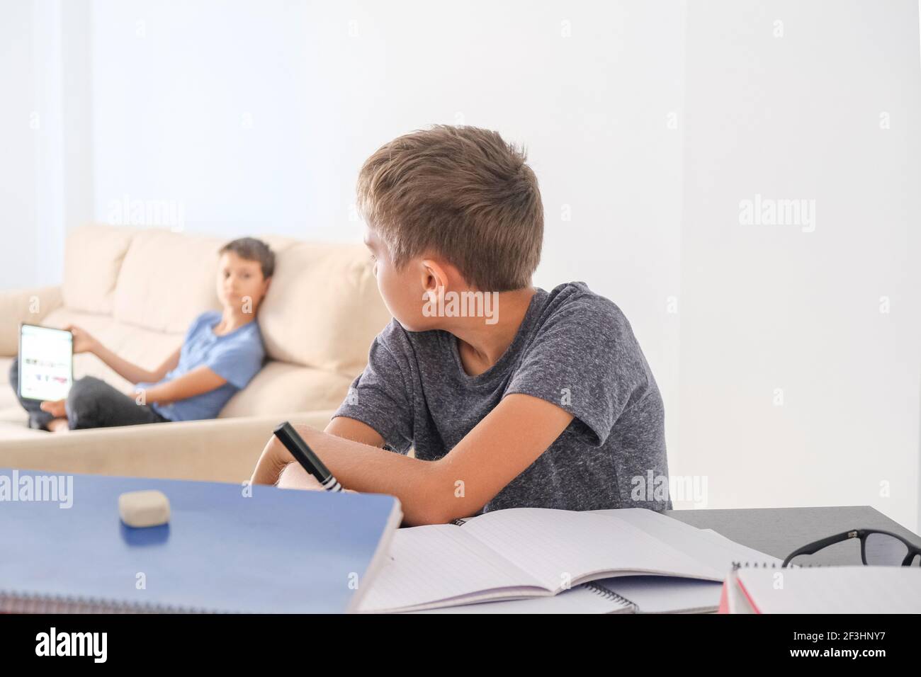 Boy doing homework with books notebooks and other boy using digital ...