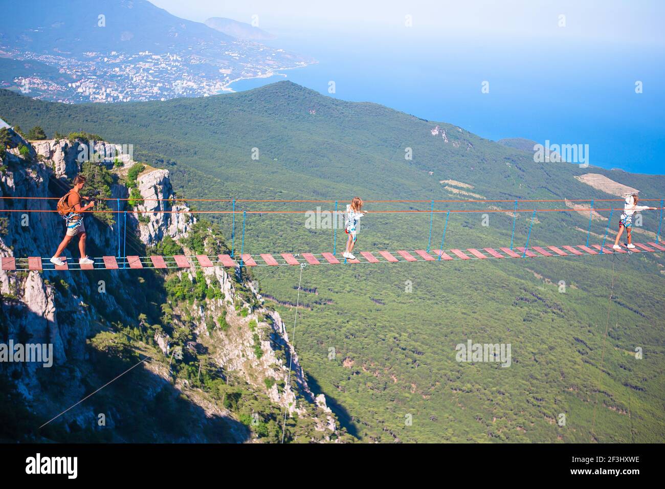 Family crossing the chasm on the rope bridge. Black sea background ...