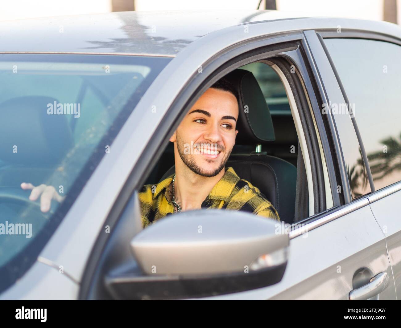 A young Spanish man smiling and driving a car Stock Photo - Alamy