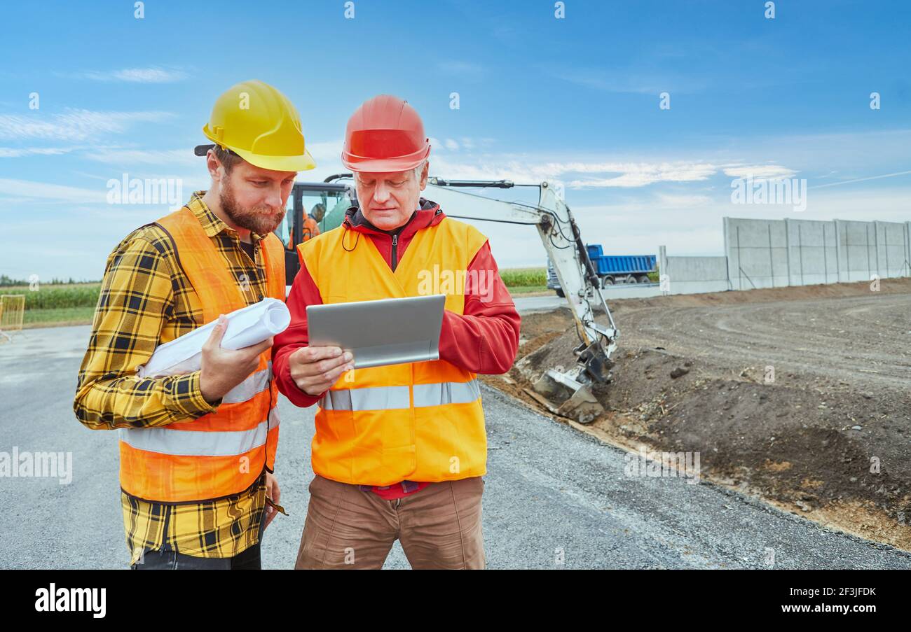 Two construction workers using tablet computer during road development ...