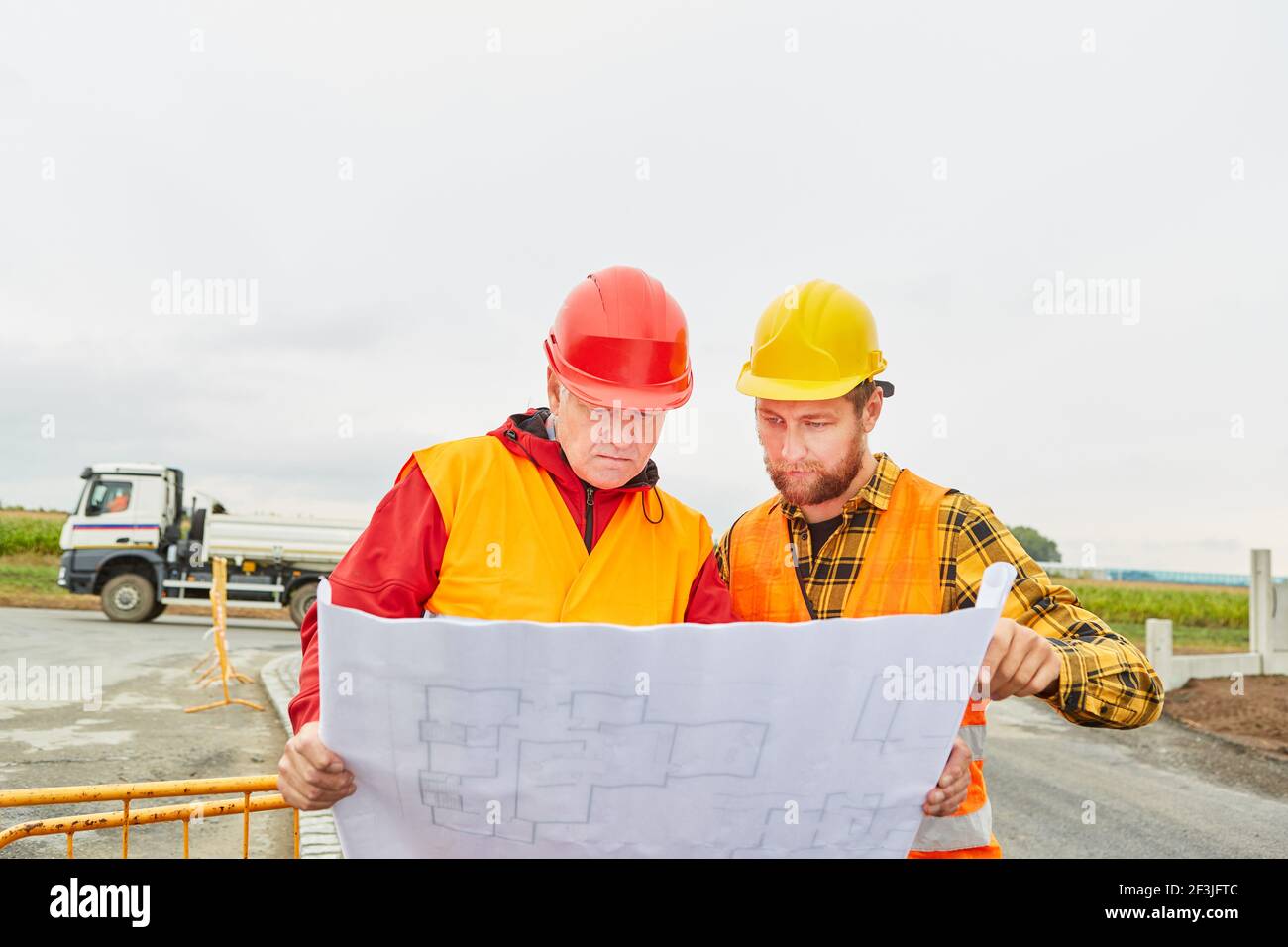 Two construction workers look at a floor plan on the construction site ...
