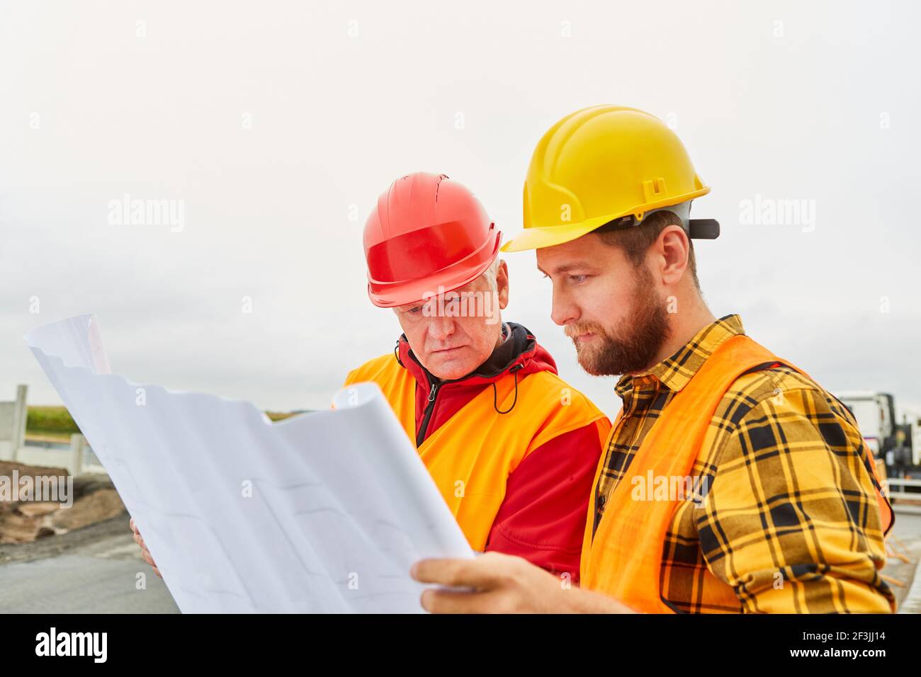 Construction workers look together at a construction plan on the road ...