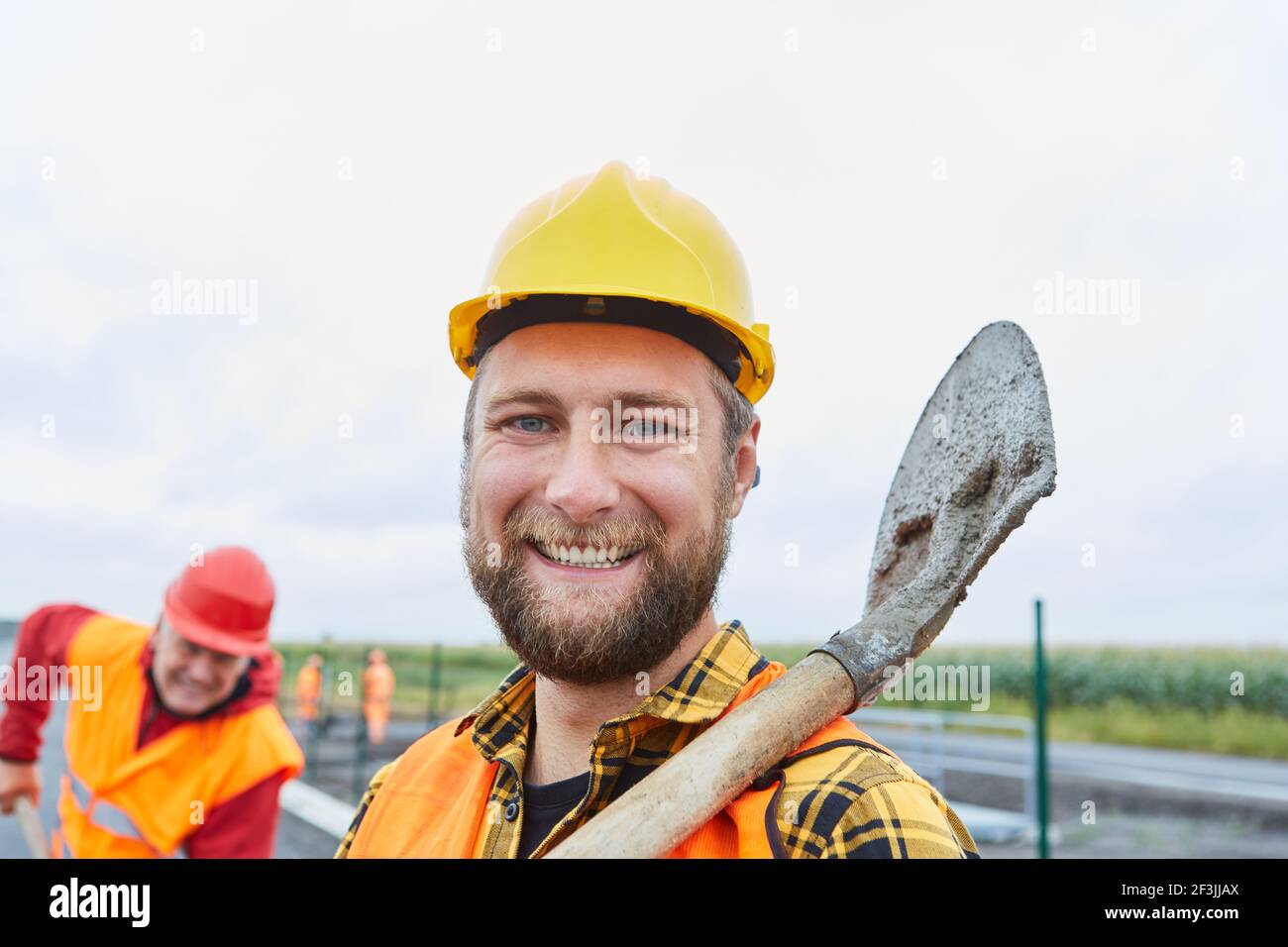 Smiling road builder with hard hat and shovel on road construction site ...