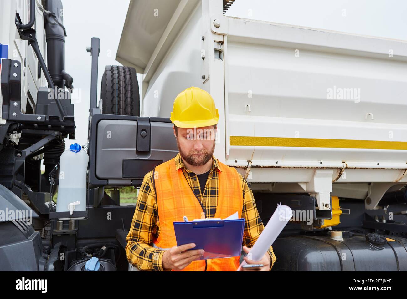 Worker with checklist checking a delivery truck at road construction ...