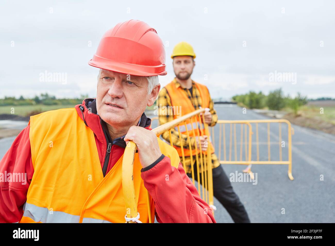 Two construction workers carry barriers on the road to secure the ...