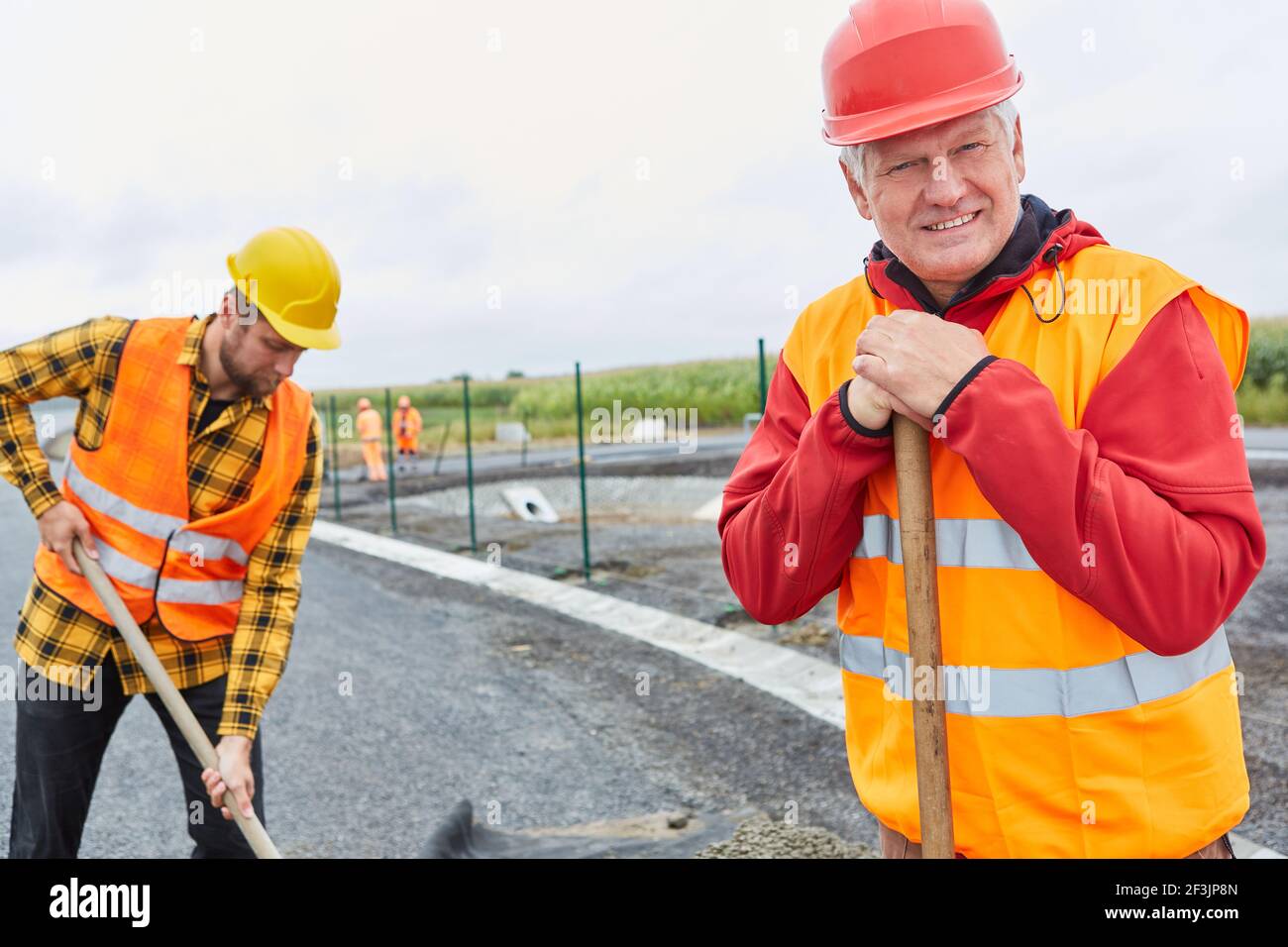 Senior construction worker and a colleague shovel concrete while ...