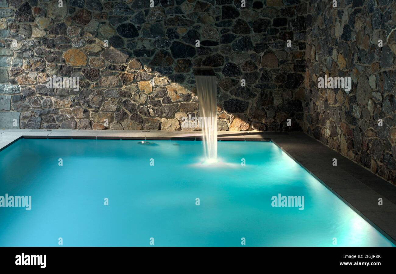 Indoor swimming pool with fountain stream of water and stone surround ...