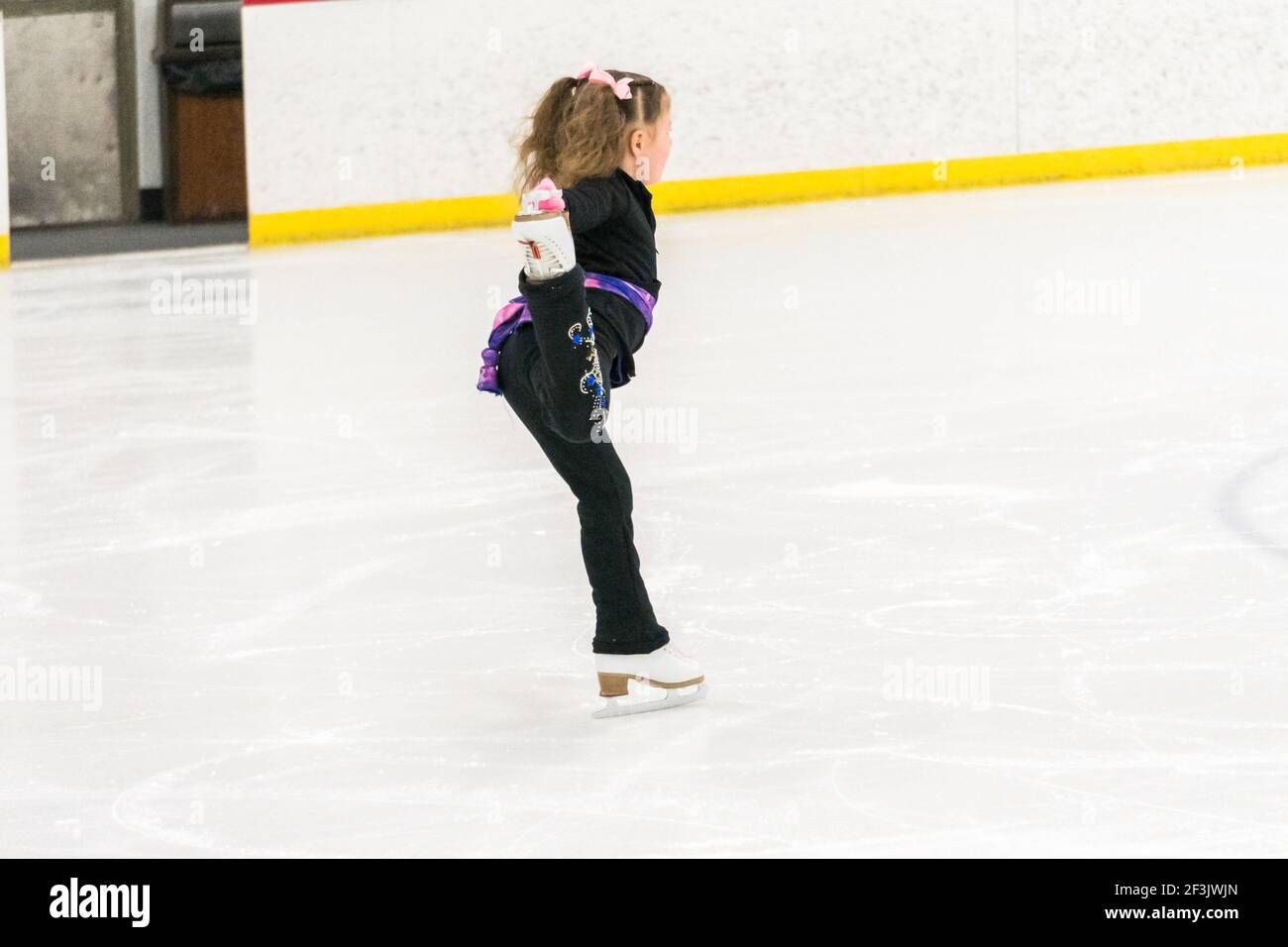 Little girl practicing figure skating moves on the indoor ice rink ...