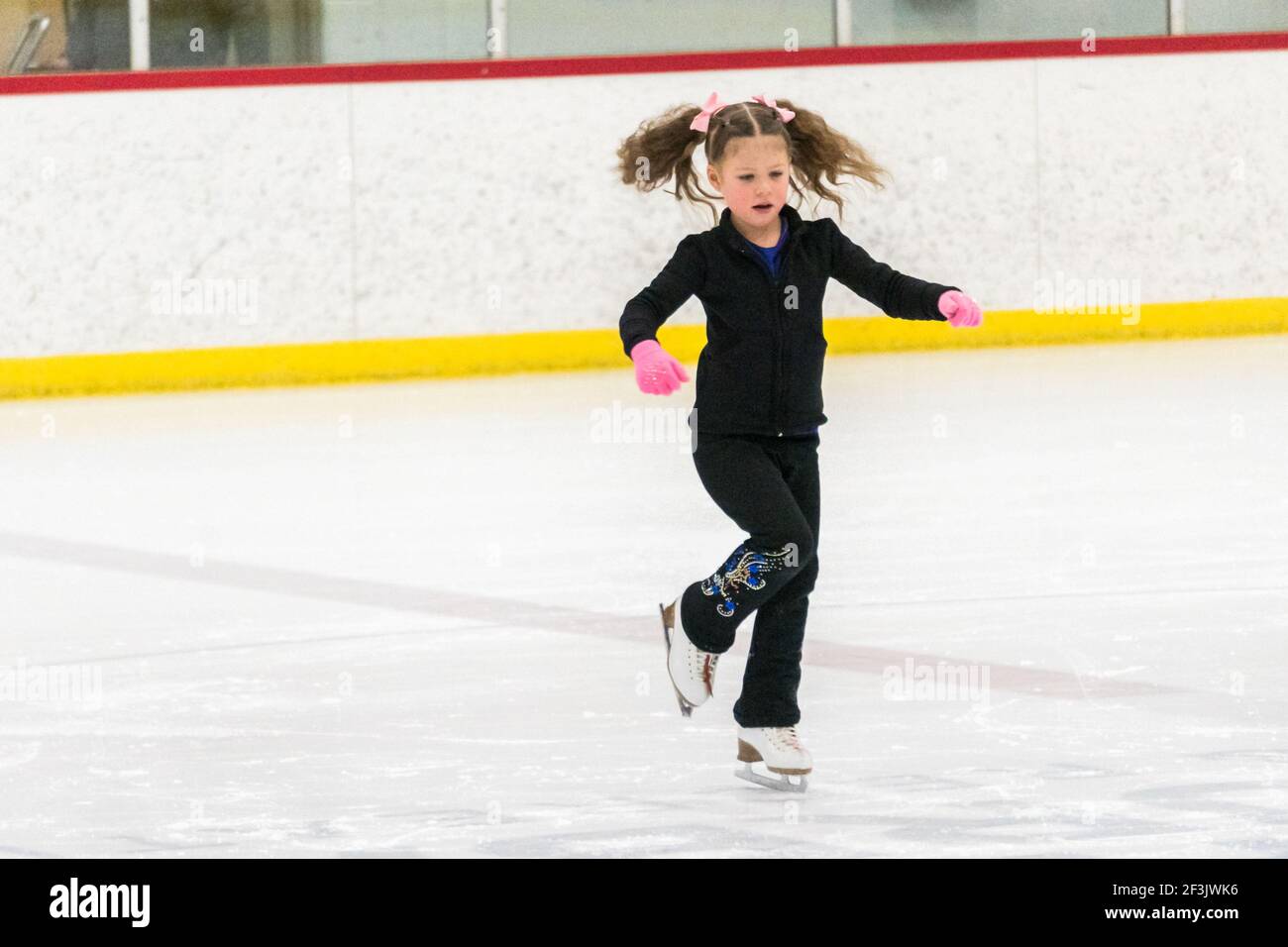 Little girl practicing figure skating moves on the indoor ice rink ...