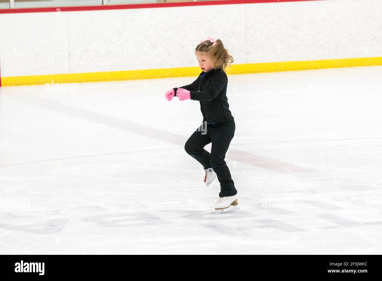 Little girl practicing figure skating moves on the indoor ice rink ...