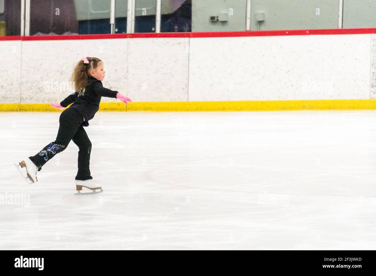 Little girl practicing figure skating moves on the indoor ice rink ...