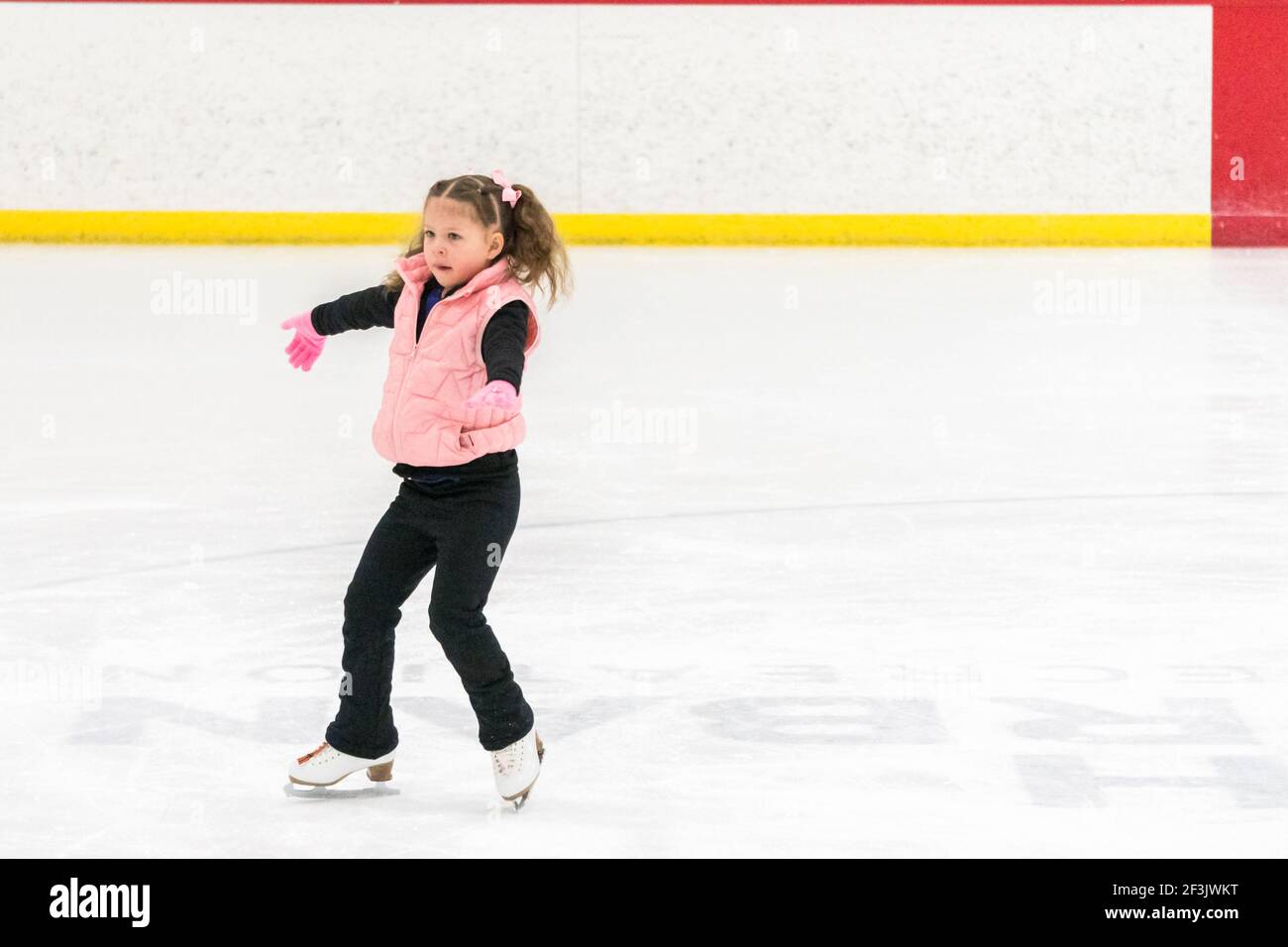 Little girl practicing figure skating moves on the indoor ice rink ...