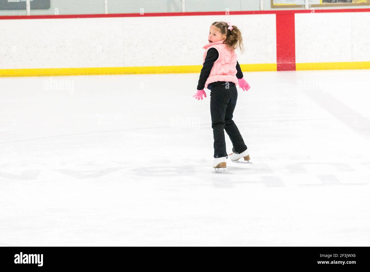 Little girl practicing figure skating moves on the indoor ice rink ...
