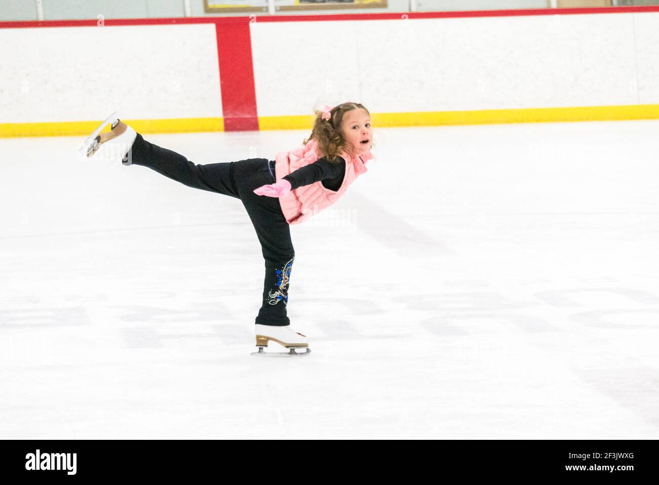 Little girl practicing figure skating moves on the indoor ice rink ...