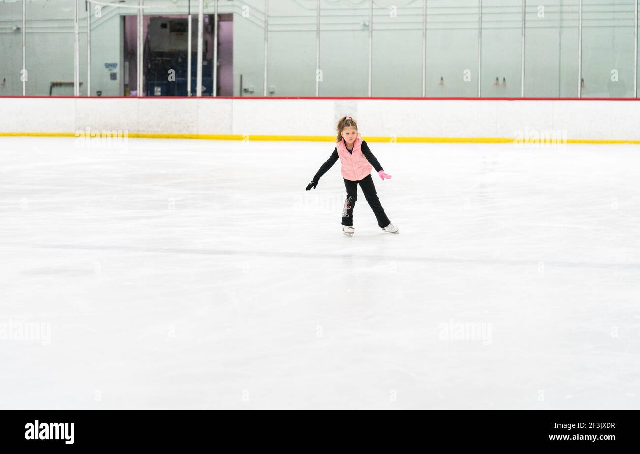 Little girl practicing figure skating elements on indoor ice skating ...