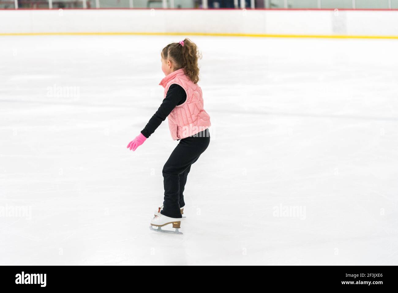 Little girl practicing figure skating elements on indoor ice skating ...