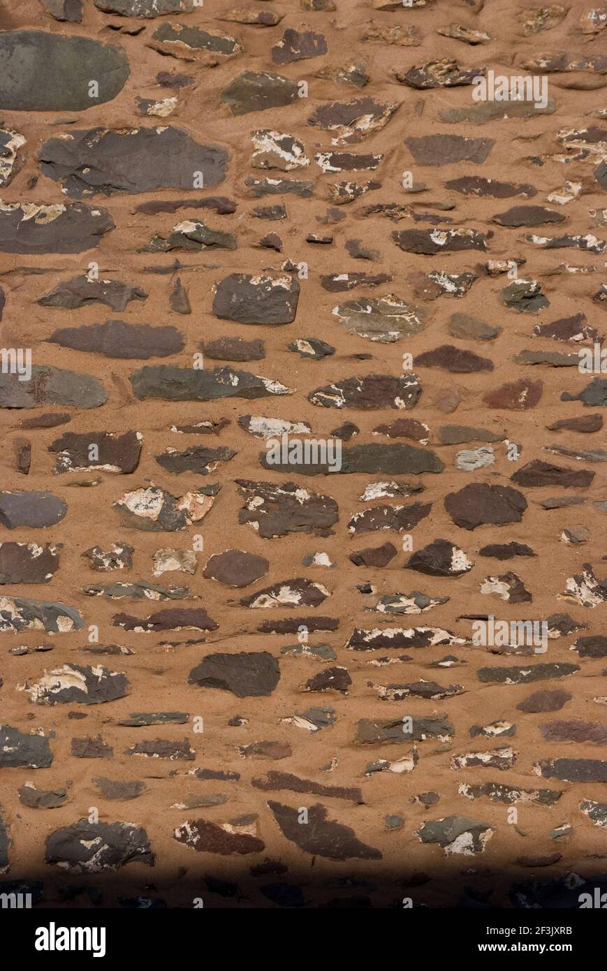 Red wall embedded with different coloured stones and rocks of a house ...