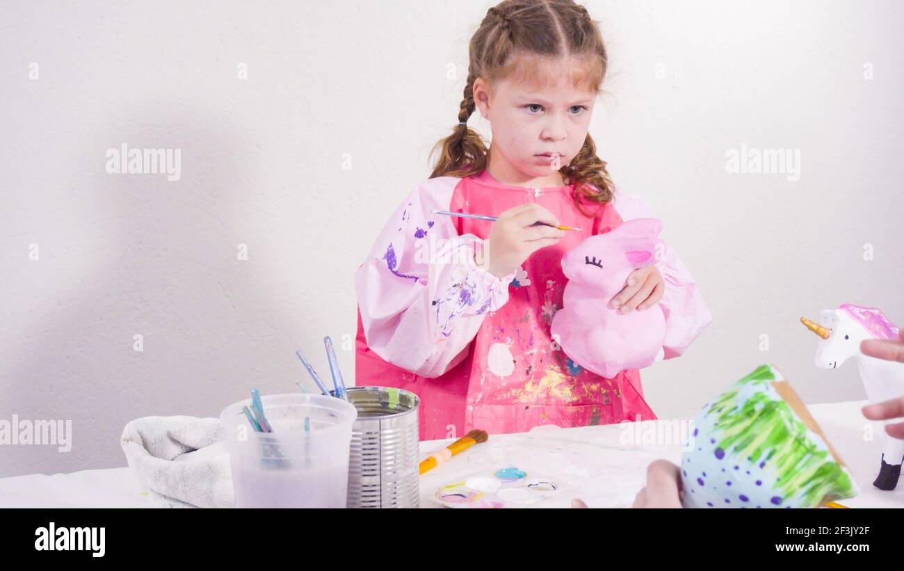 Little girl painting paper mache figurines with acrylic paint for her ...