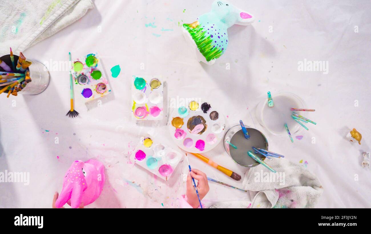 Flat lay. Little girl painting paper mache figurines with acrylic paint ...