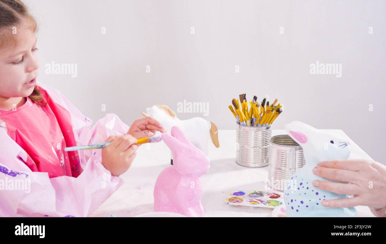 Little girl painting paper mache figurines with acrylic paint for her ...