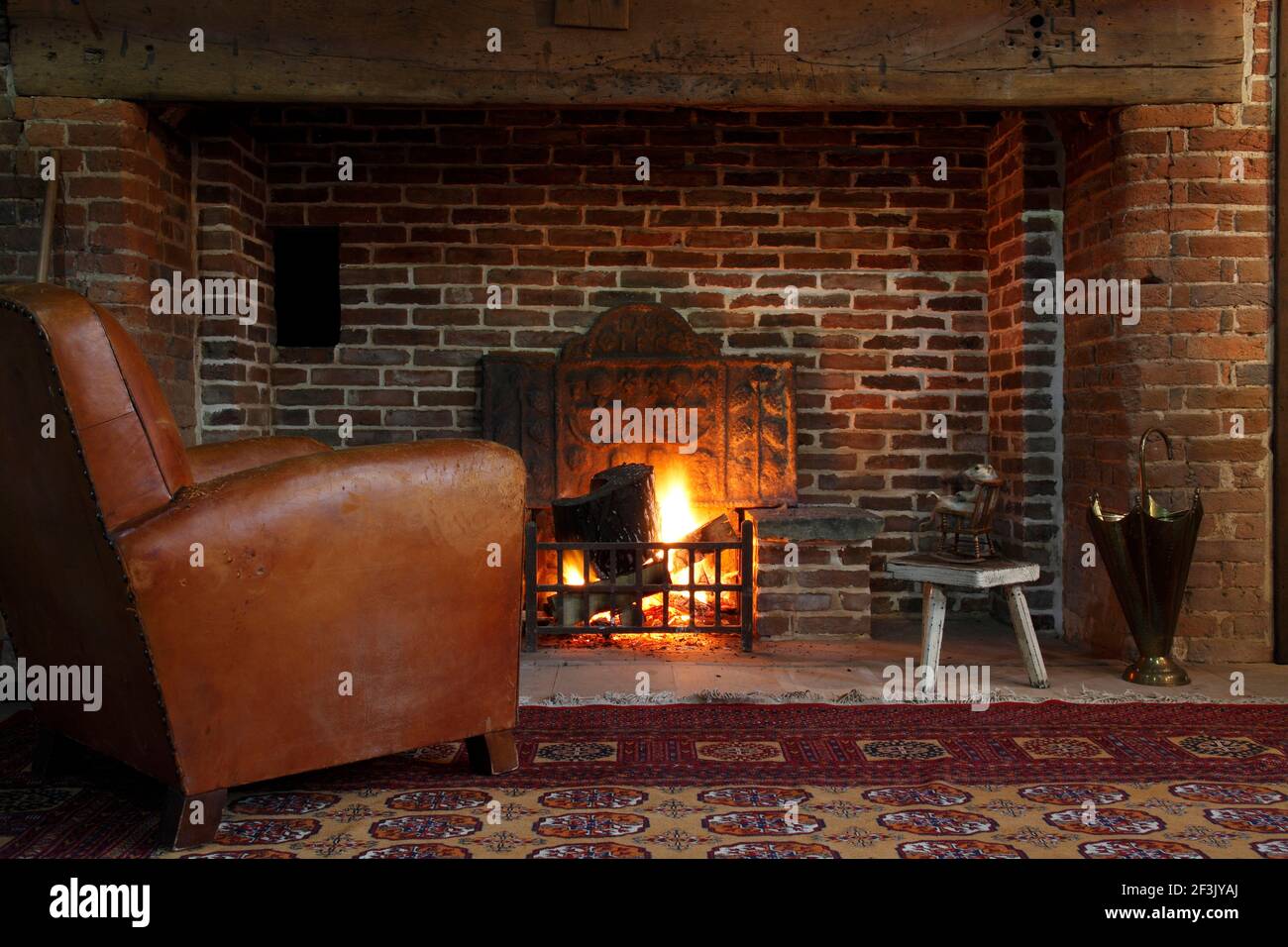 Old leather armchair in front of roaring fire in inglenook with oak ...