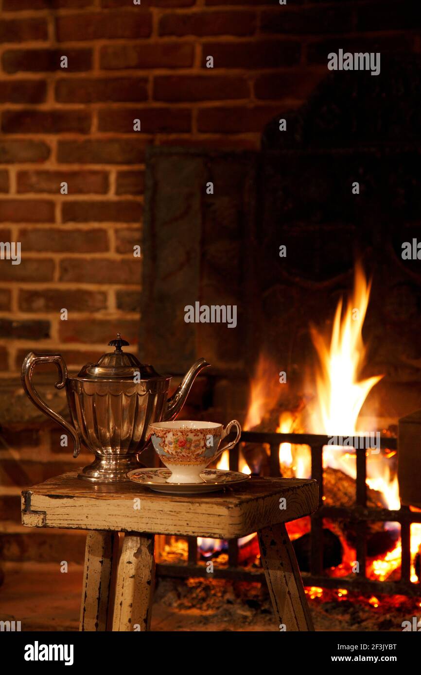 Close up of silver teapot and cup and saucer in front of roaring pub ...