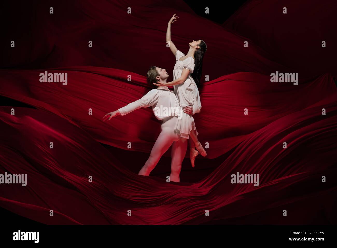 Wine. Young and graceful ballet dancers on red cloth background in ...