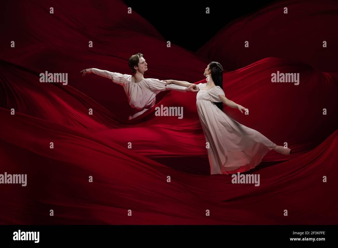 Light. Young and graceful ballet dancers on red cloth background in classic action. Art, motion ...