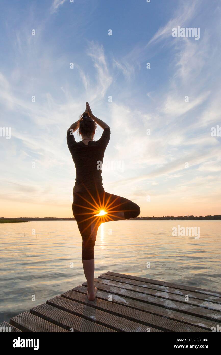 Woman doing yoga exercises on a jetty by a lake, Tree pose. Schleswig ...