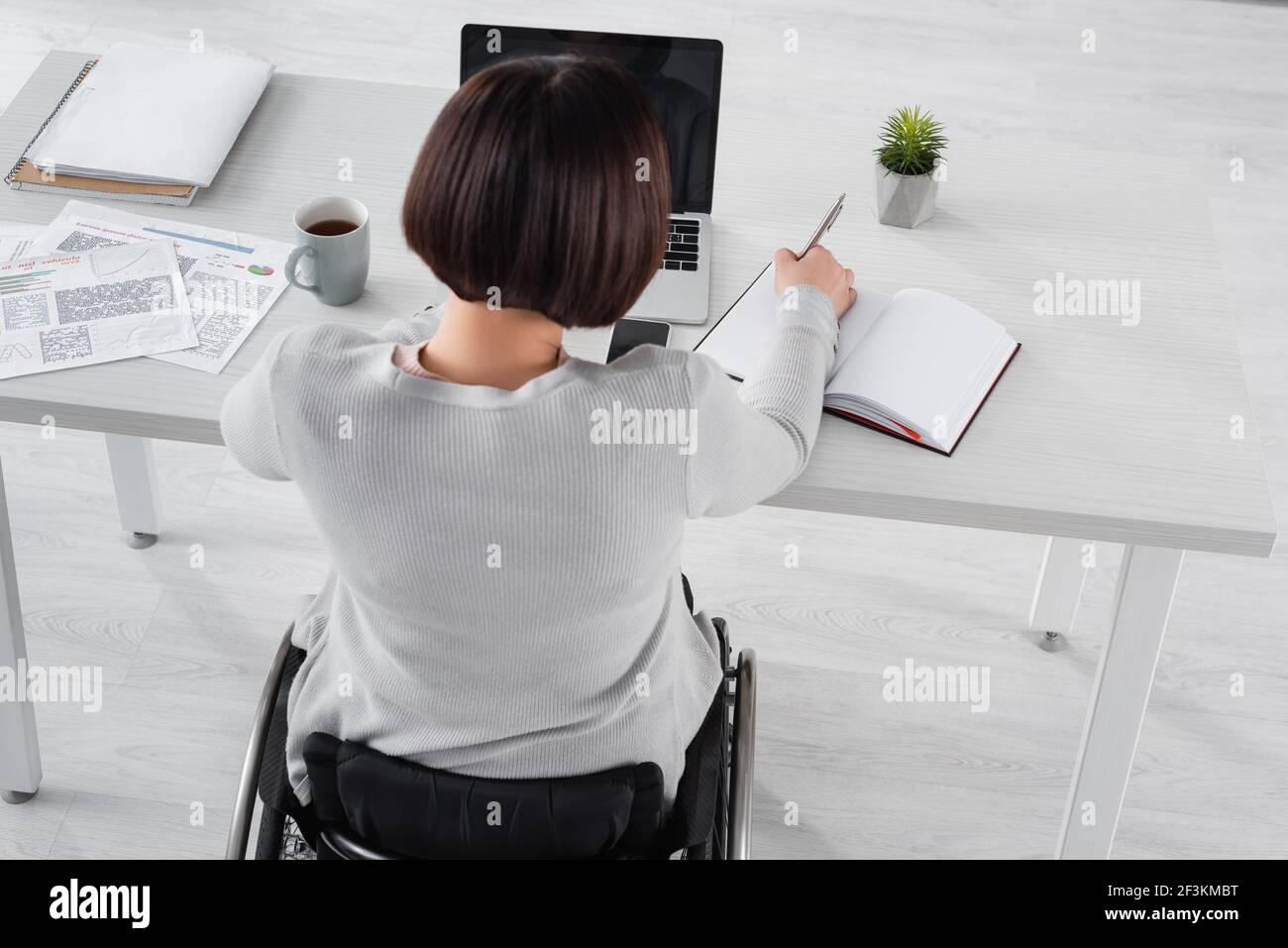 Overhead view of freelancer in wheelchair writing on notebook near ...