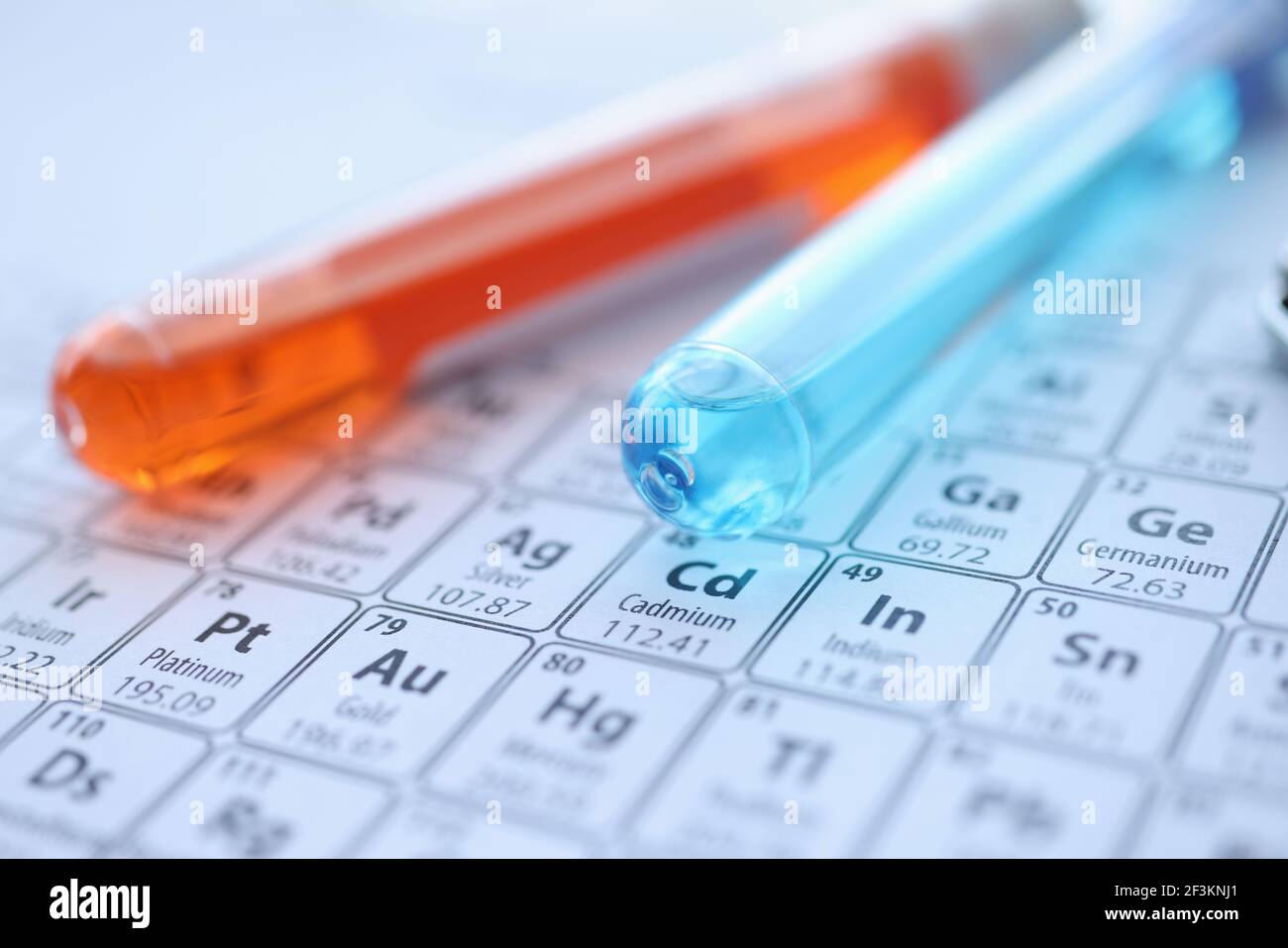 Two test tubes with colored reagents lying on periodic table closeup ...