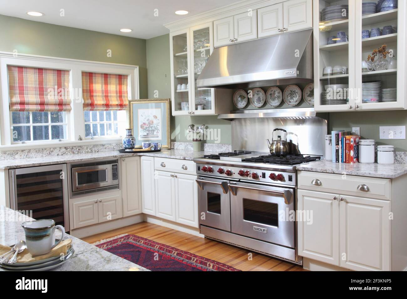 Bright white kitchen with large stainless steel gas range and hood ...