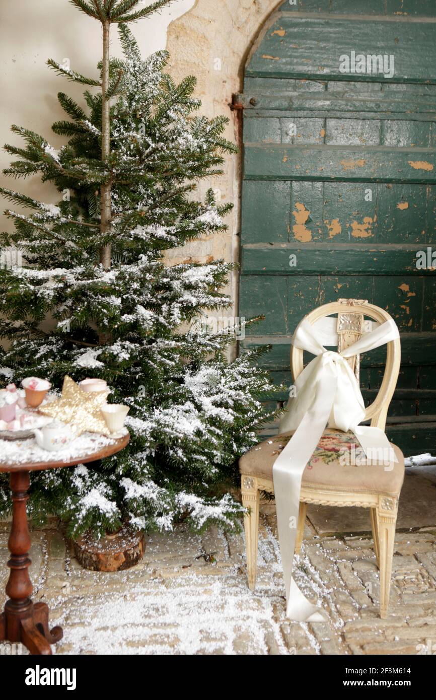 Chair with ribbon bow in front of Christmas tree with artificial snow ...