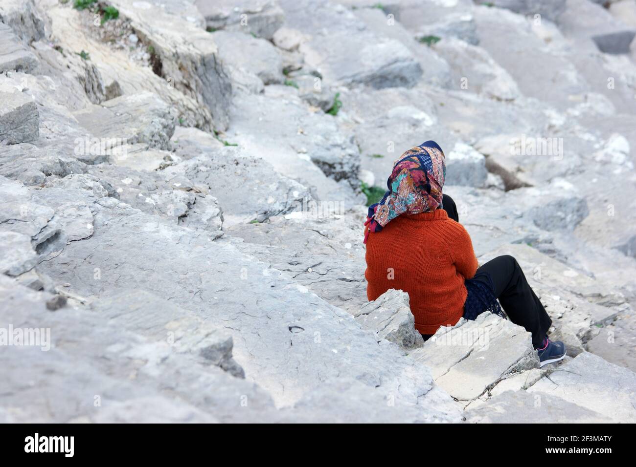 Back view of woman in headscarf sitting on the rocks Stock Photo - Alamy